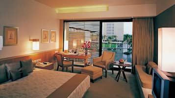 Quarto de hotel com cama, escrivaninha, poltrona, sofá e televisão.