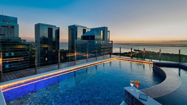 Piscina infinita no terraço, com vista para a cidade, rodeada por edifícios modernos.