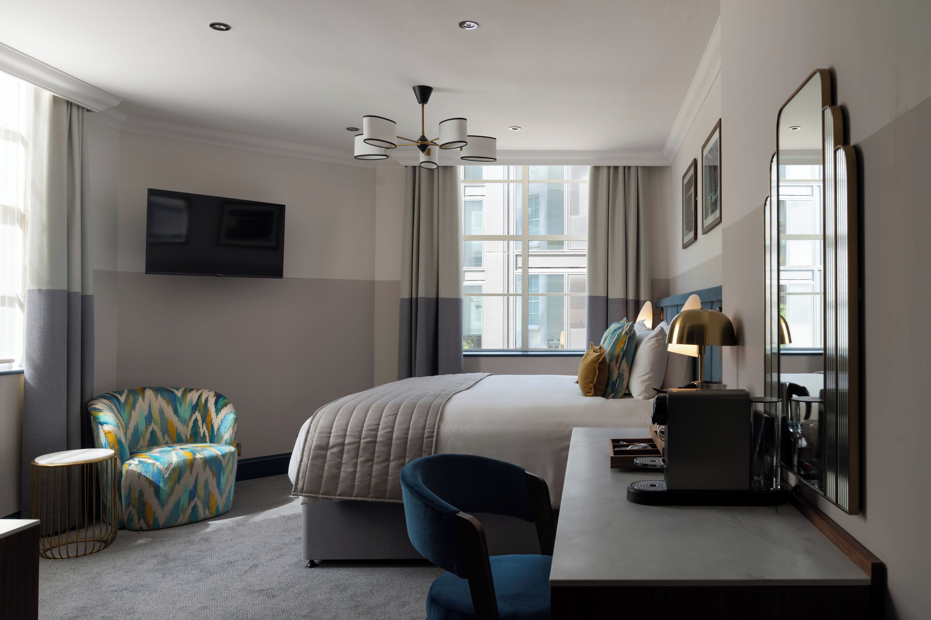 Quarto de hotel moderno com uma cama grande, uma escrivaninha, uma cadeira, uma televisão e uma janela com cortinas.