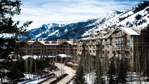 Um hotel de vários andares com estilo arquitetônico tradicional, rodeado por montanhas cobertas de neve e pinheiros.