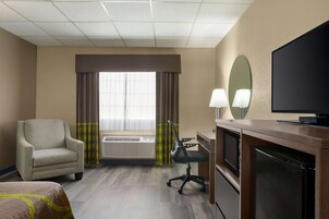 Quarto de hotel com cama, escrivaninha com computador, televisão, aparelho de ar condicionado e janela com cortinas.