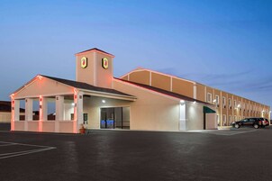 Um motel com estrutura térrea, balcão coberto e estacionamento.