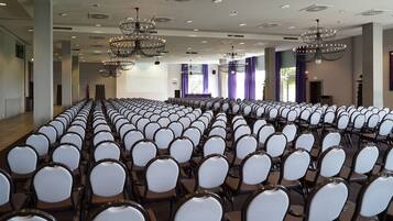 Uma sala de conferências com fileiras de cadeiras, grandes lustres e um palco.