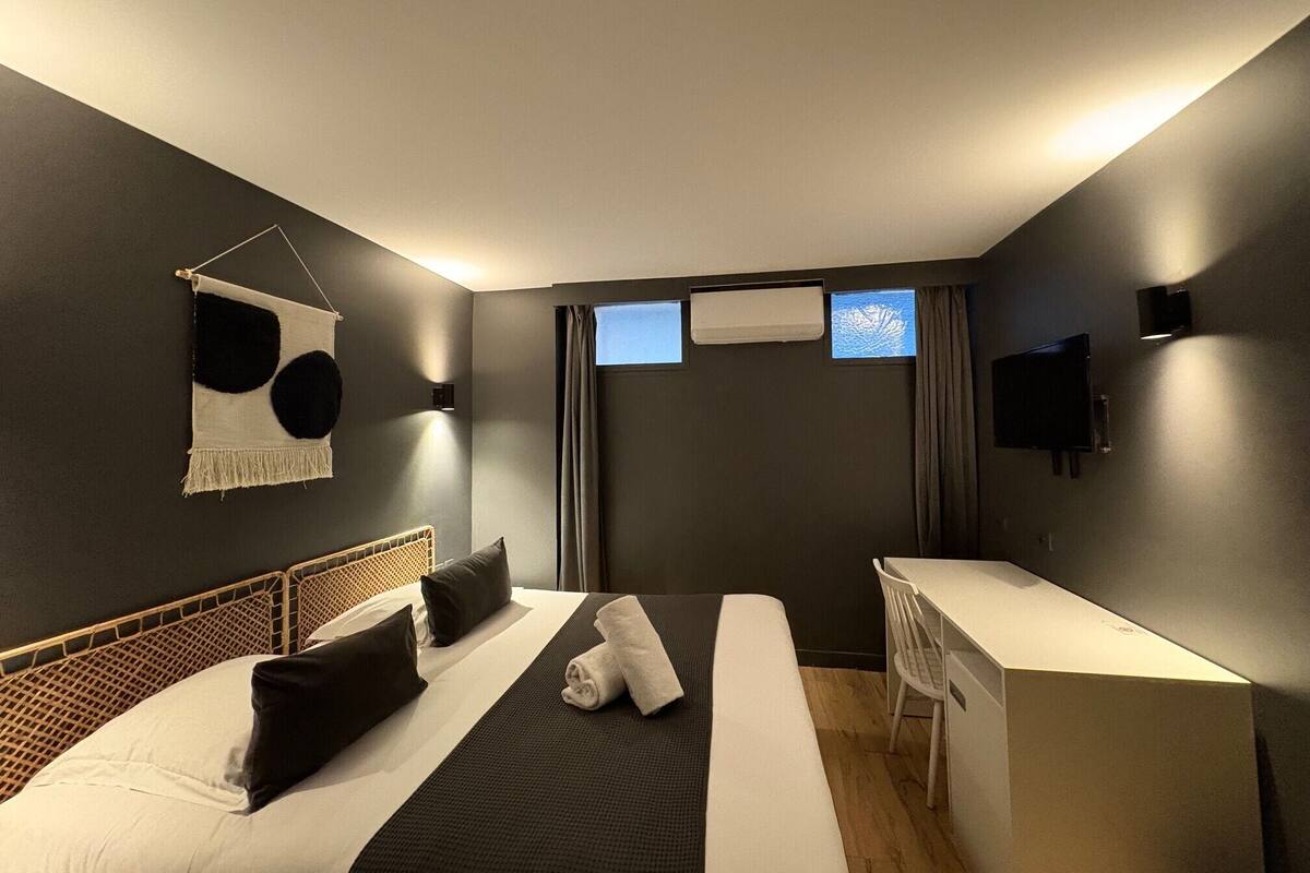 Quarto de hotel moderno com uma cama grande, uma escrivaninha e uma televisão.