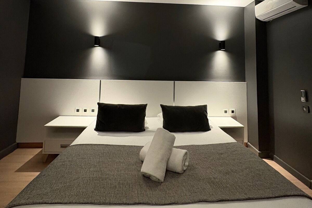 Quarto de hotel moderno com uma cama grande, duas mesas de cabeceira e um ar condicionado integrado.