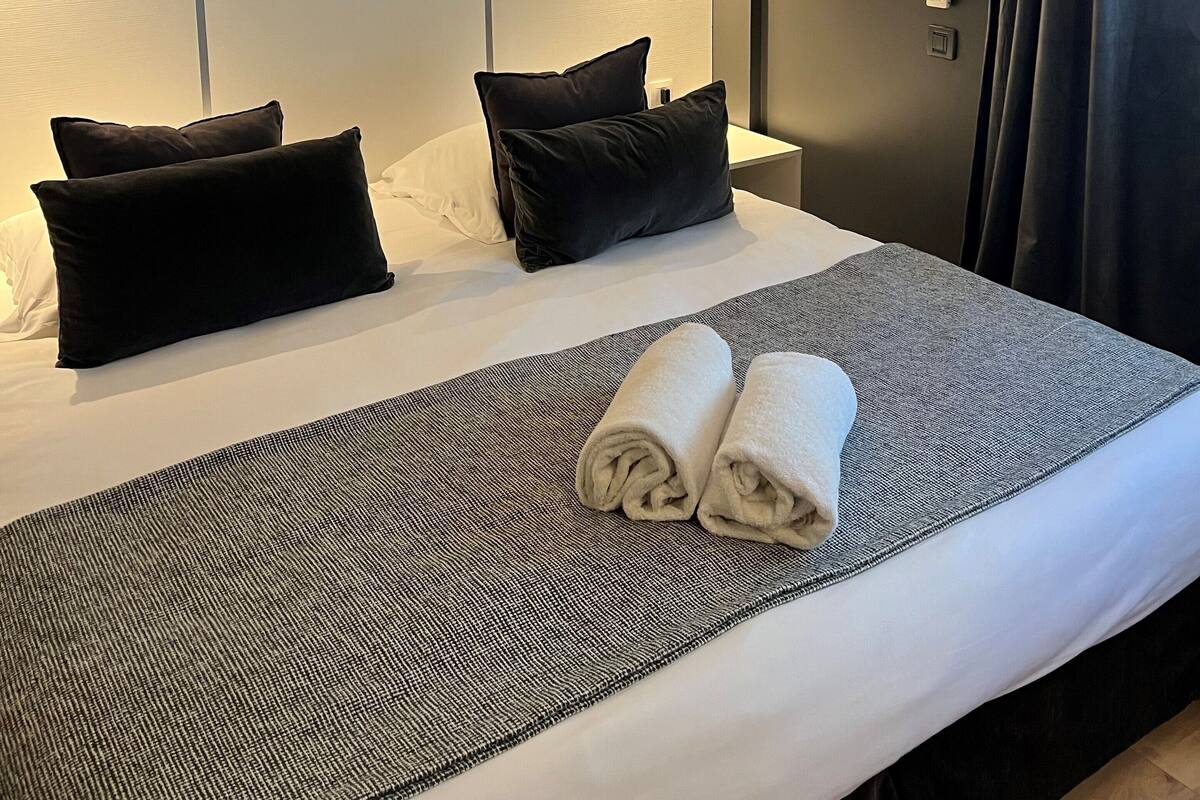 Quarto de hotel moderno com uma cama grande, paredes escuras e um ar condicionado.