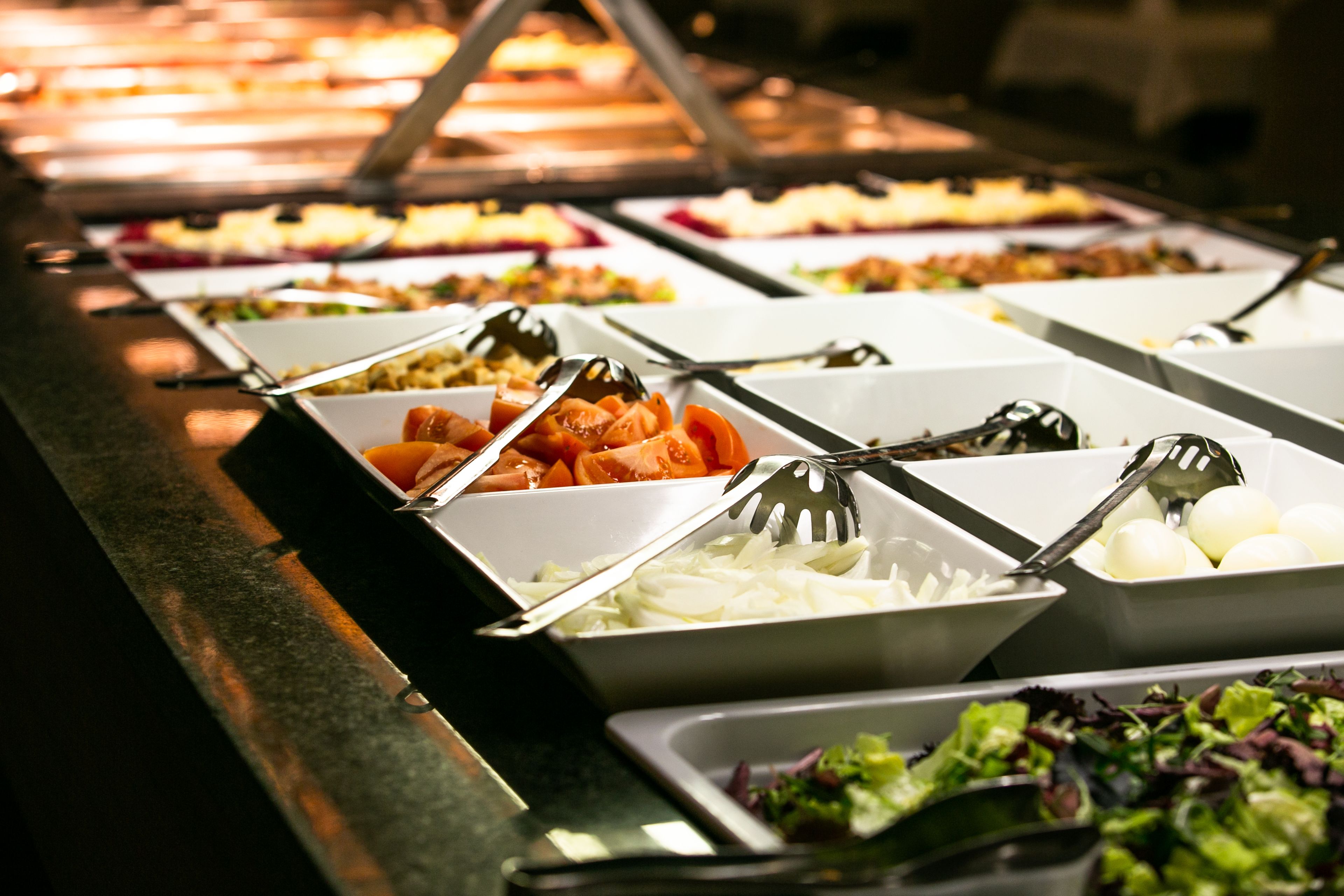 Buffet com diversas opções de comida, incluindo legumes, carnes e saladas.