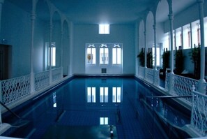 Uma piscina interior com vista clara, cercada por colunas e grades brancas, e uma grande janela na extremidade.
