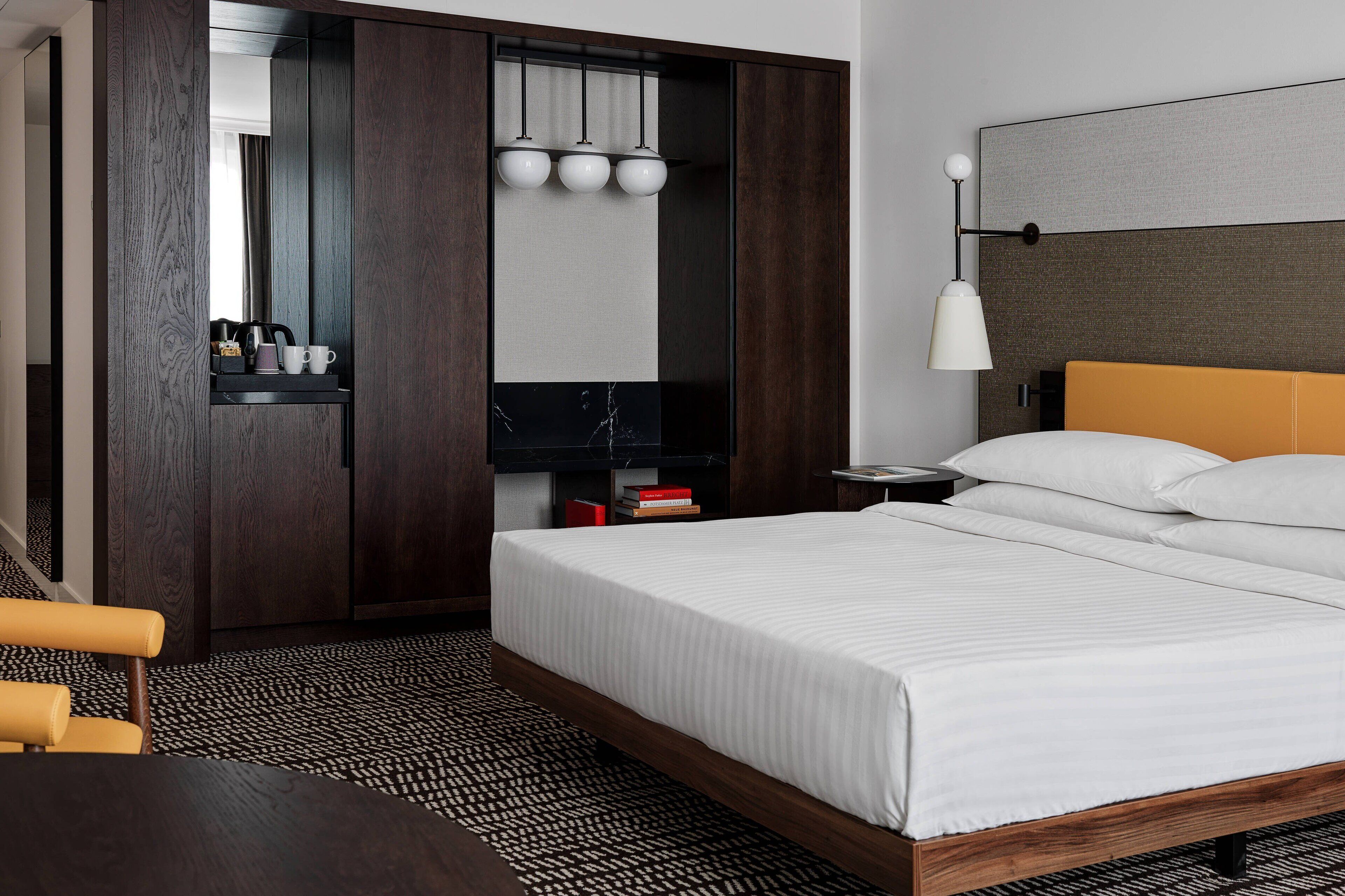 Quarto de hotel com uma cama grande, um guarda-roupa de madeira, uma mesinha e um espelho.