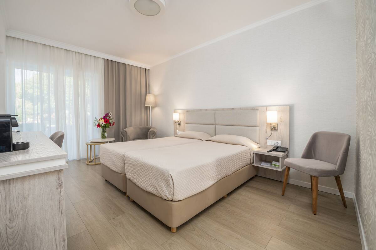 Quarto de hotel com uma cama grande, uma escrivaninha com computador, uma cadeira, um abajur e uma mesa de cabeceira.