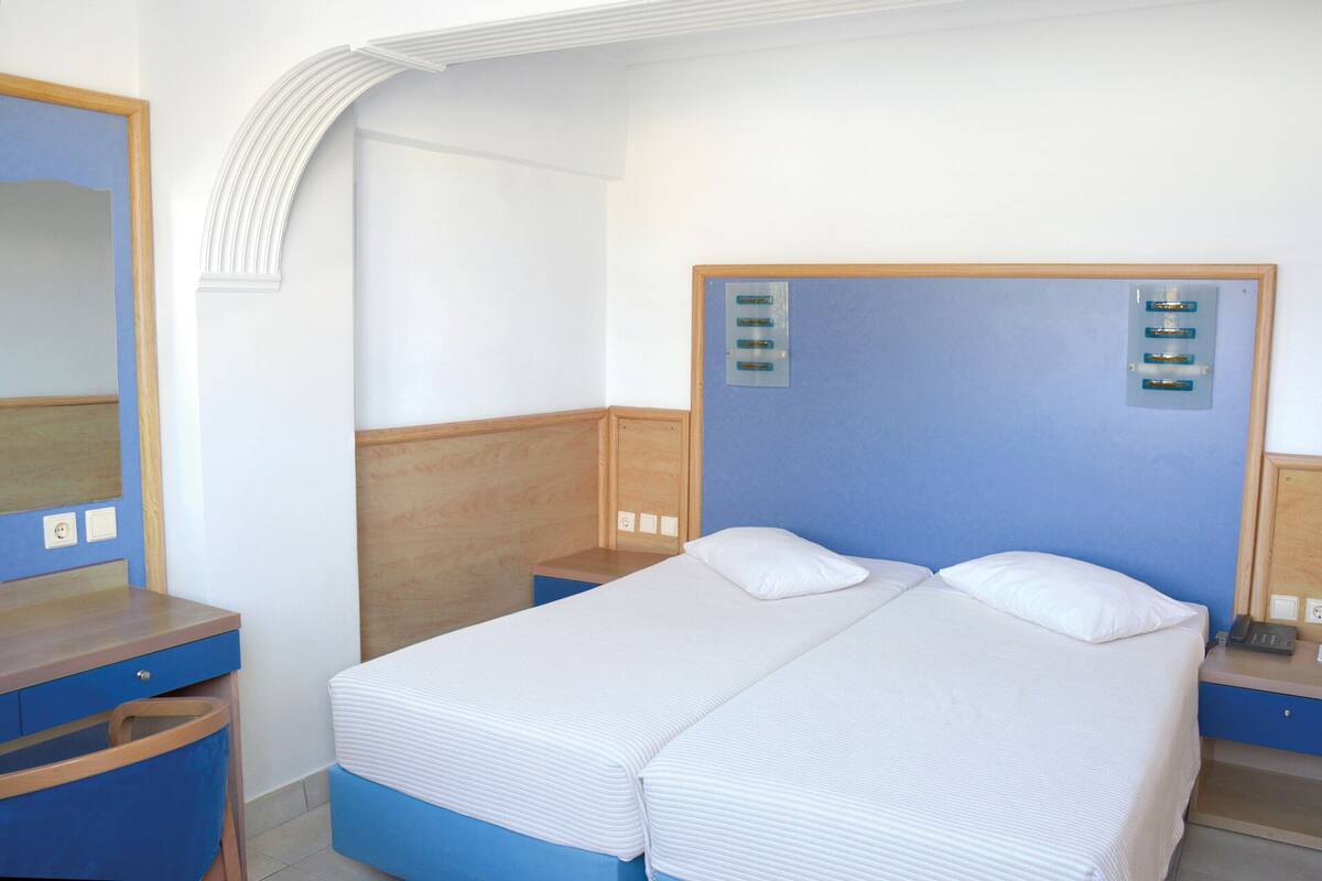 Cama de casal com cabeceira de madeira e parede azul decorativa. Há uma mesa de cabeceira com um telefone e um abajur.