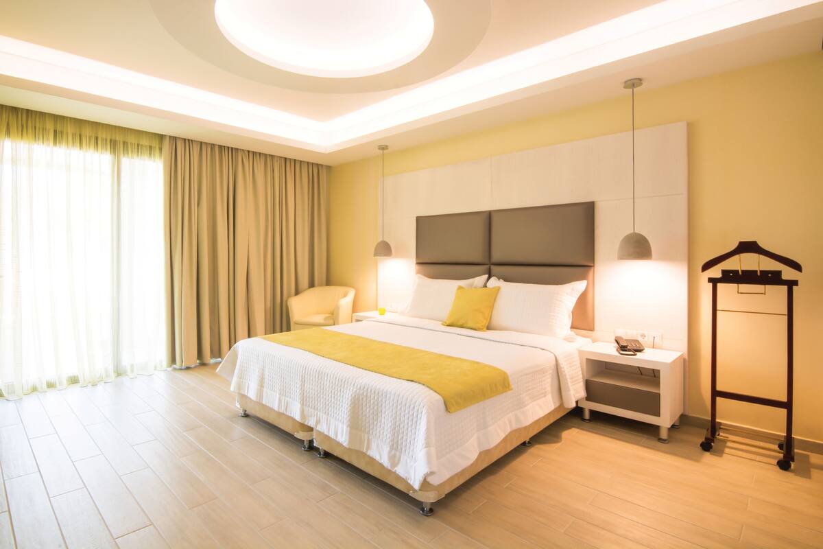Quarto de hotel moderno com uma cama grande, mesas de cabeceira, uma cadeira e um guarda-roupa.