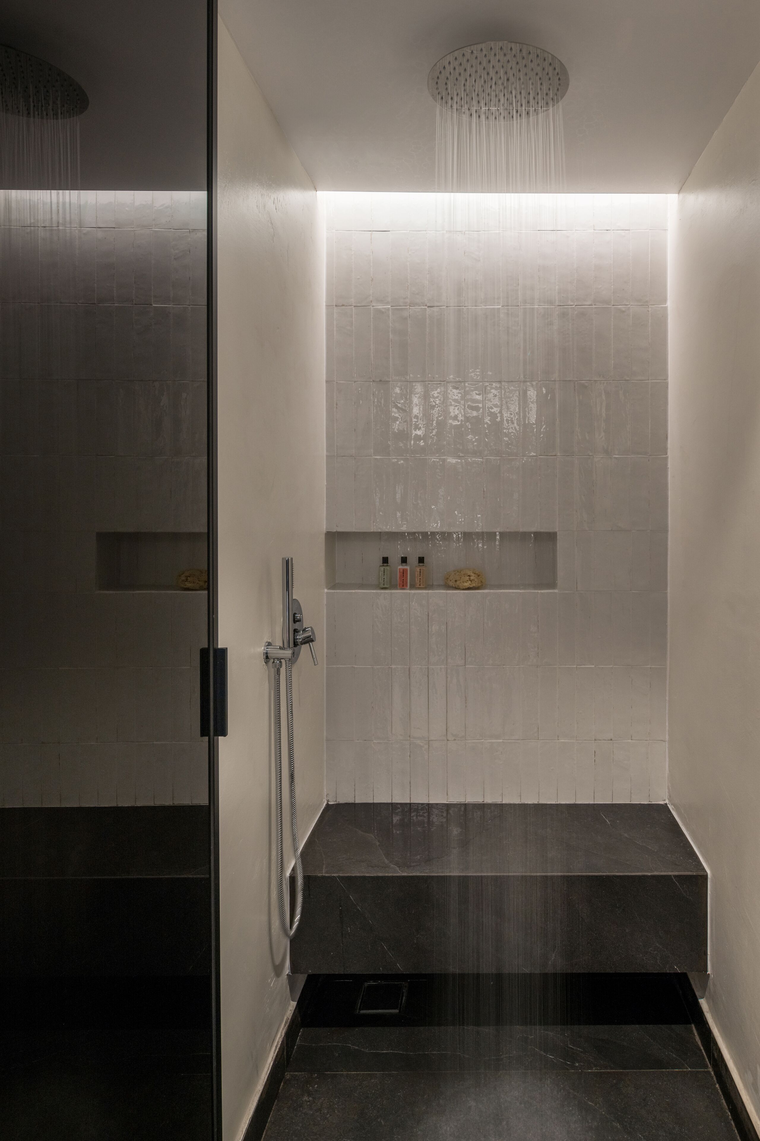 Uma área de chuveiro moderna com divisória de vidro, prateleira embutida com artigos de higiene pessoal e chuveiro de chuva.
