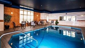Piscina interior com paredes azulejadas, diversos tipos de assentos e plantas em vasos.