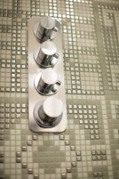Painel de controle com quatro botões metálicos sobre uma superfície revestida de azulejos.
