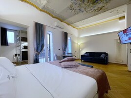 Quarto de hotel com cama, sofá, escrivaninha e televisão.