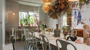 Uma sala de jantar com uma mesa comprida, várias cadeiras e diversos vasos de plantas.