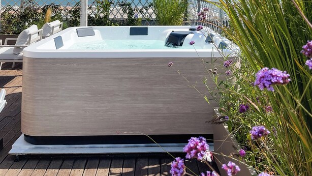 Uma banheira de hidromassagem com um deck de madeira e uma pérgula, com vista para uma praia.