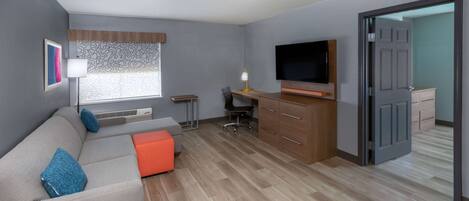 Uma sala de estar moderna com um sofá, um banquinho e uma TV fixada na parede.
