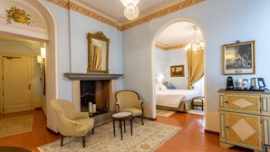 Quarto de hotel com lareira, duas poltronas, uma cama e uma cômoda.