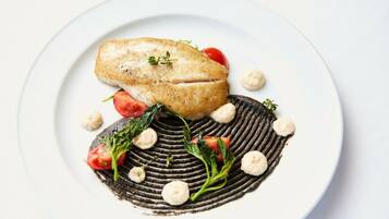 Um prato com um pedaço de peixe, tomates cereja e um molho escuro com padrão circular.