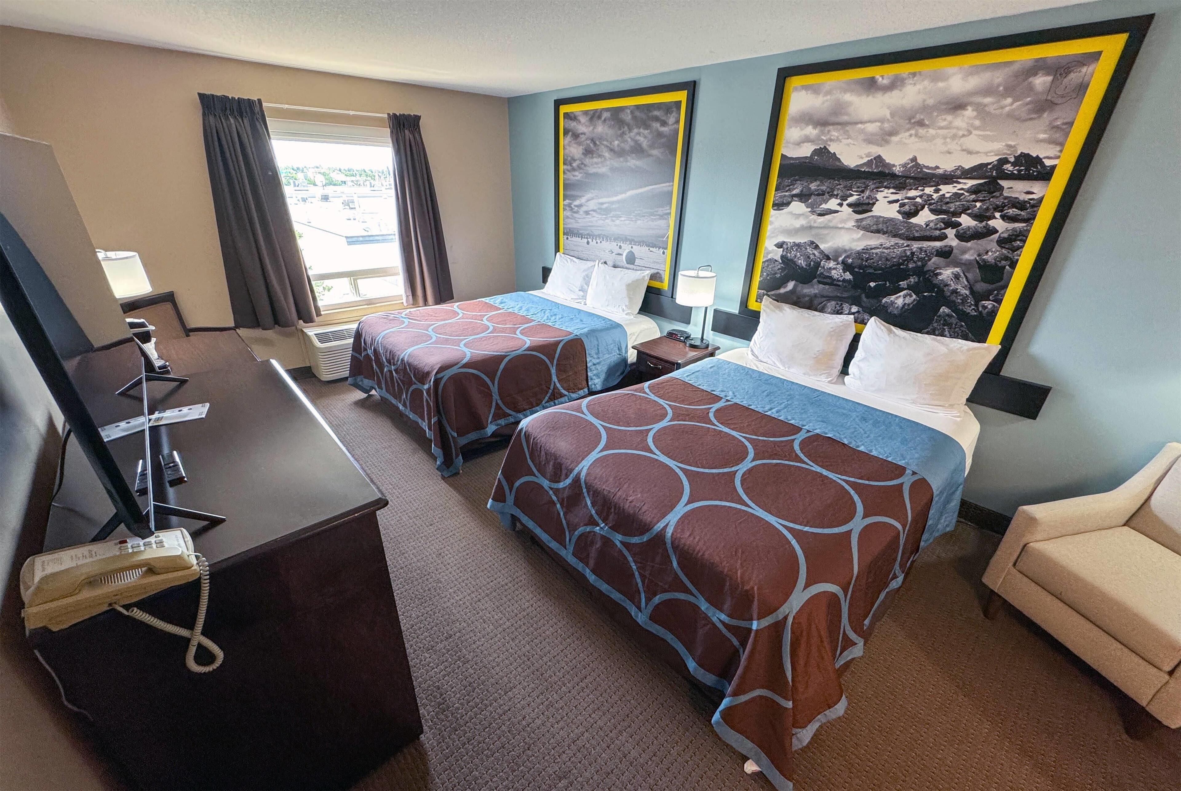Quarto de hotel com duas camas, uma escrivaninha com telefone e uma cadeira.