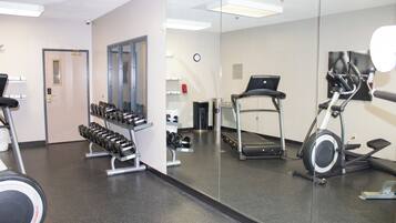 Academia com equipamentos de ginástica, incluindo esteiras, halteres e um espelho grande na parede.
