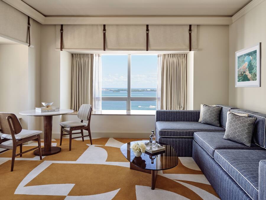 Uma sala de estar moderna com sofá, cadeiras, mesa de centro e vista para o mar.