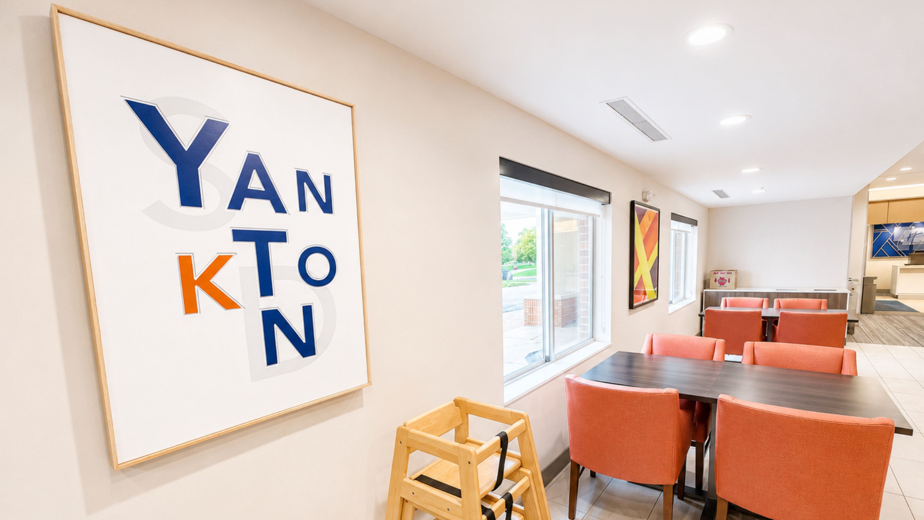 Decoração moderna com um quadro grande, área de jantar com cadeiras laranja e vista pela janela.