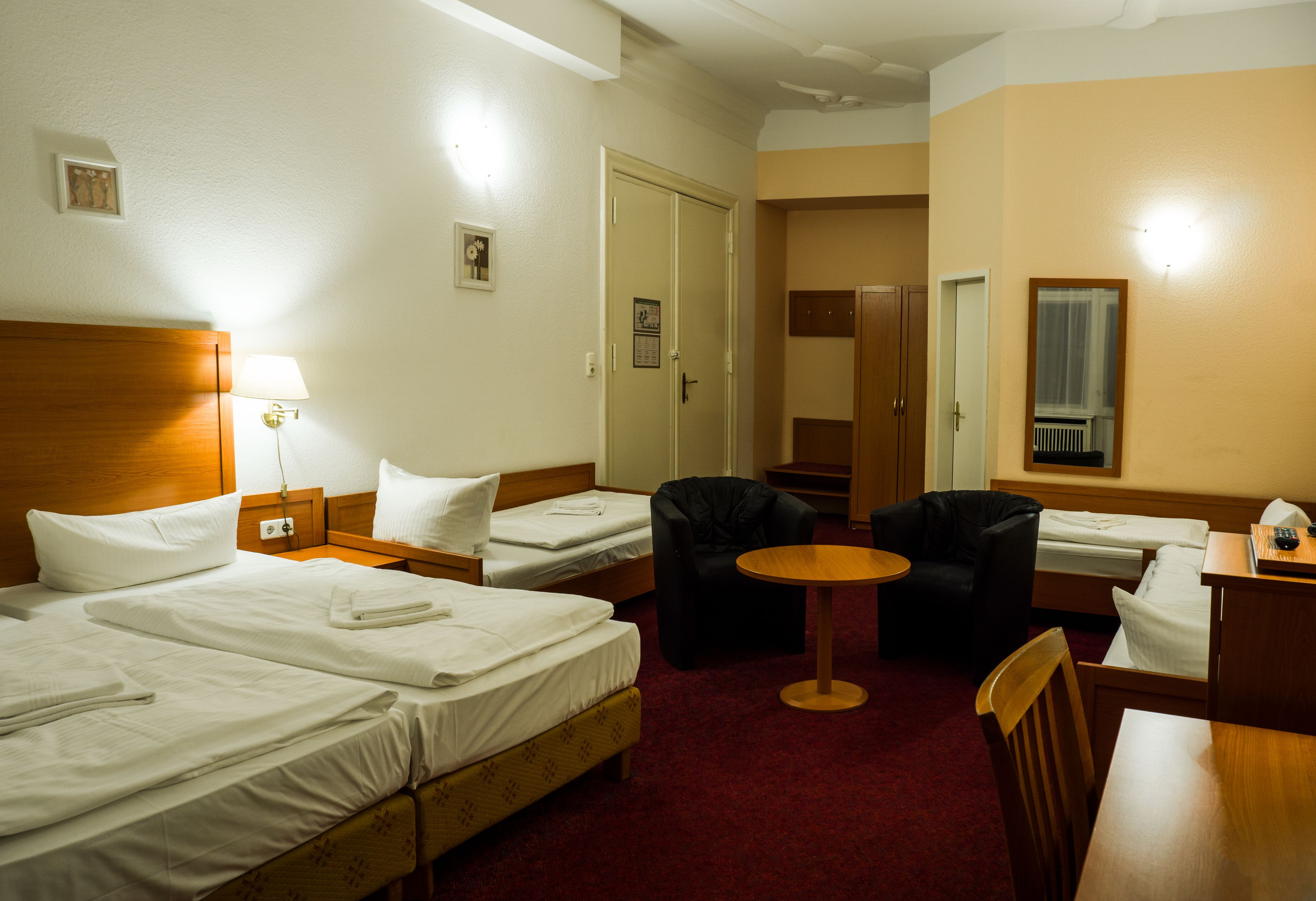Quarto de hotel com duas camas, uma mesa redonda, duas cadeiras, uma escrivaninha e um espelho.