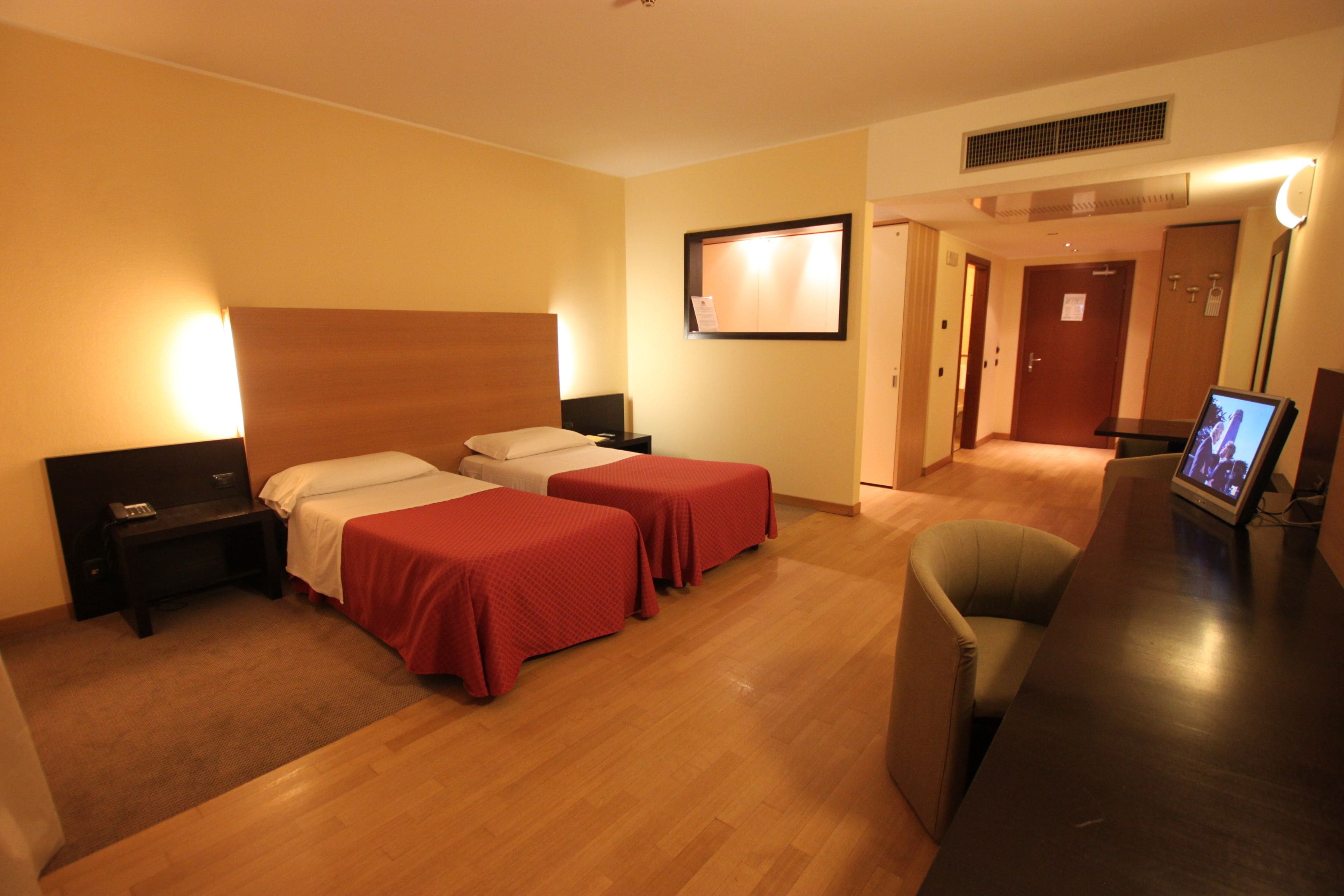 Quarto de hotel com duas camas de solteiro, uma escrivaninha com computador e uma cadeira.