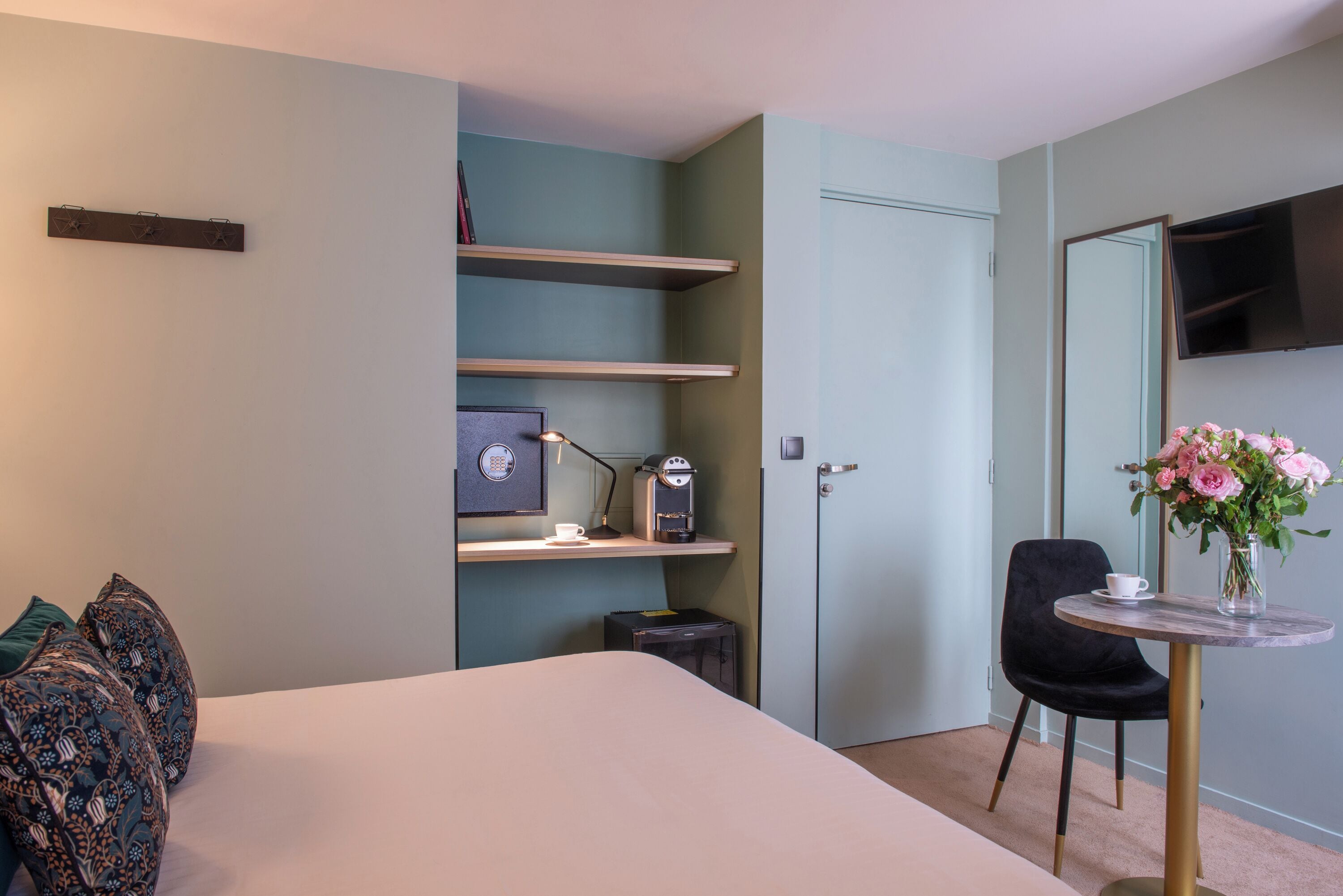 Quarto de hotel moderno com cama, escrivaninha com cafeteira, cadeira e vaso com flores.