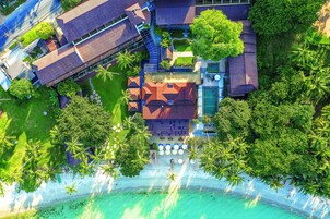 Vista aérea de um resort com praia, palmeiras e área de piscina.