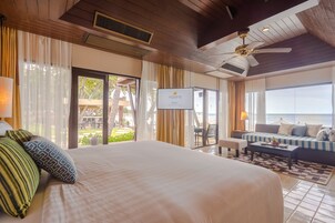 Quarto de hotel com uma cama grande, um sofá, uma TV e vista para a praia.