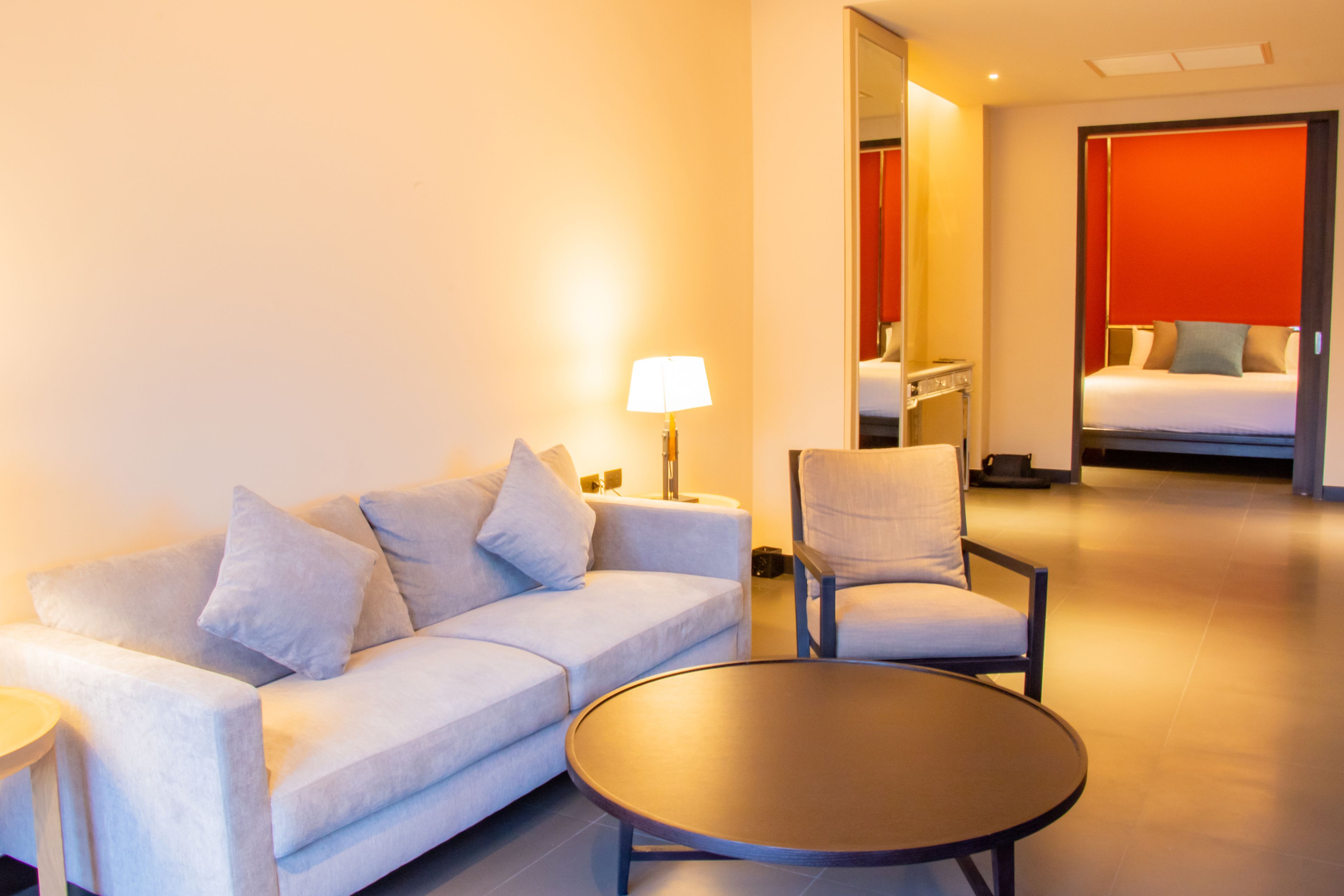 Quarto de hotel moderno com sofá, poltrona e mesa de centro redonda.