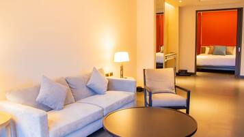 Quarto de hotel moderno com sofá, poltrona e mesa de centro redonda.