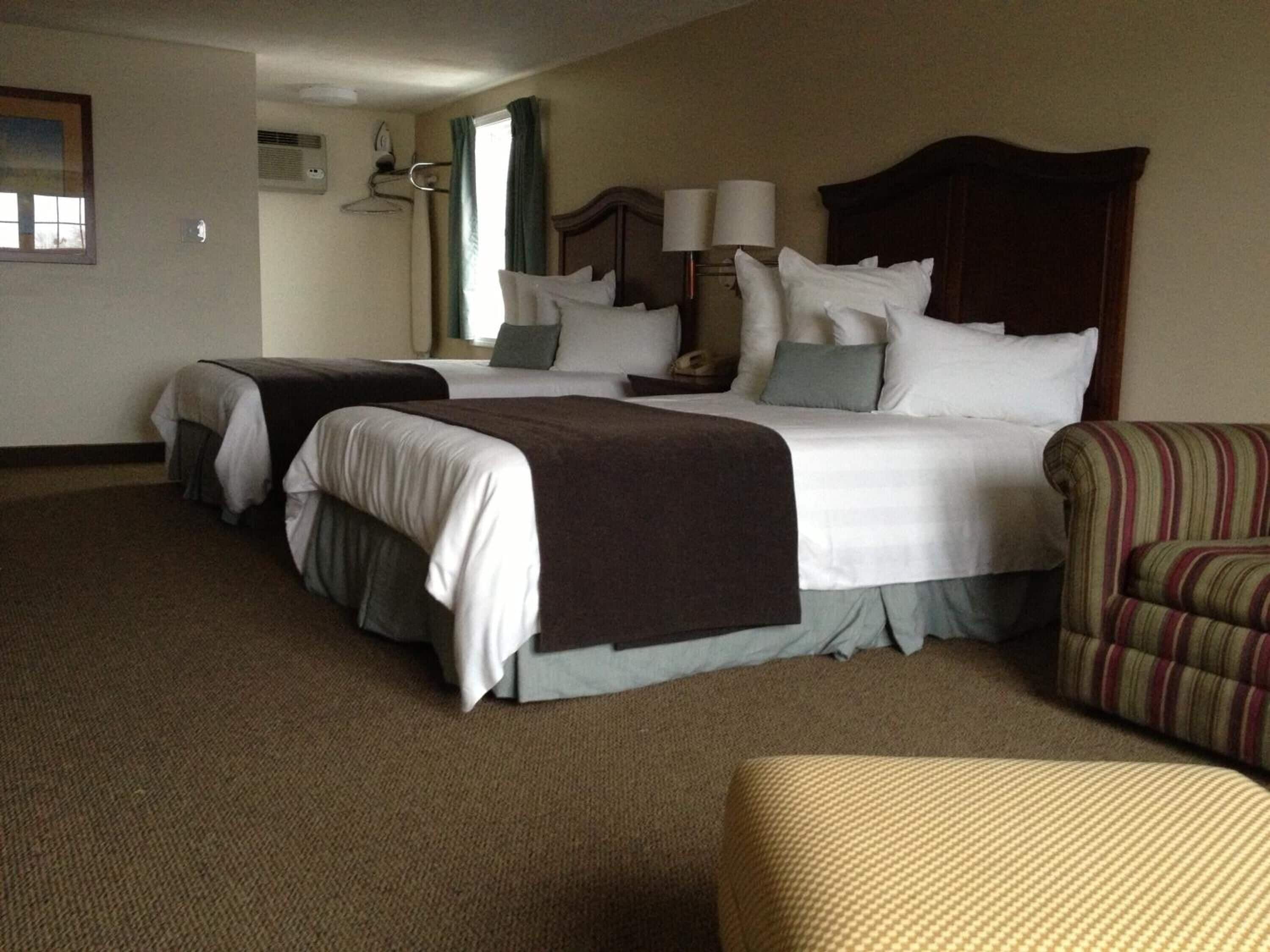 Quarto de hotel com duas camas, uma cadeira e piso coberto por carpete.
