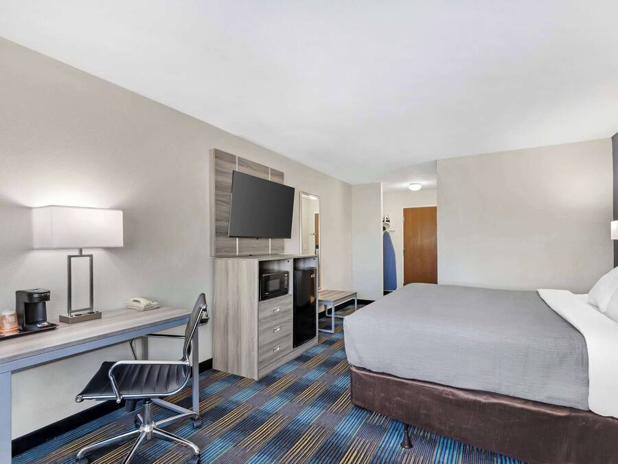 Quarto de hotel com cama, escrivaninha, cadeira, televisão, micro-ondas e uma pequena cozinha equipada.
