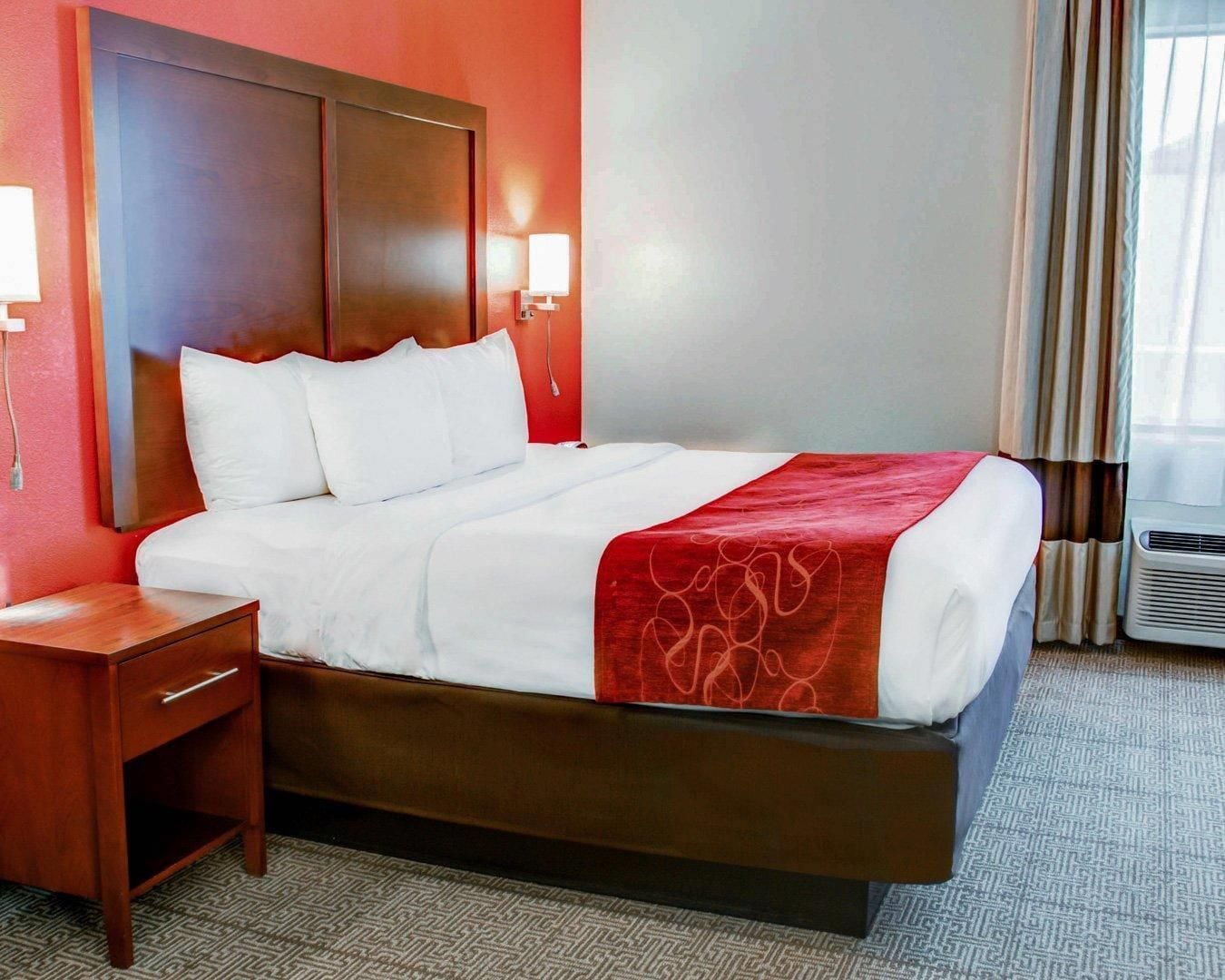 Quarto de hotel com cama, mesa de cabeceira, abajur e ar condicionado.