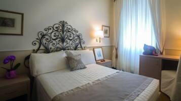 Cama bem arrumada com cabeceira decorativa, mesa de cabeceira com abajur e janela com cortinas.