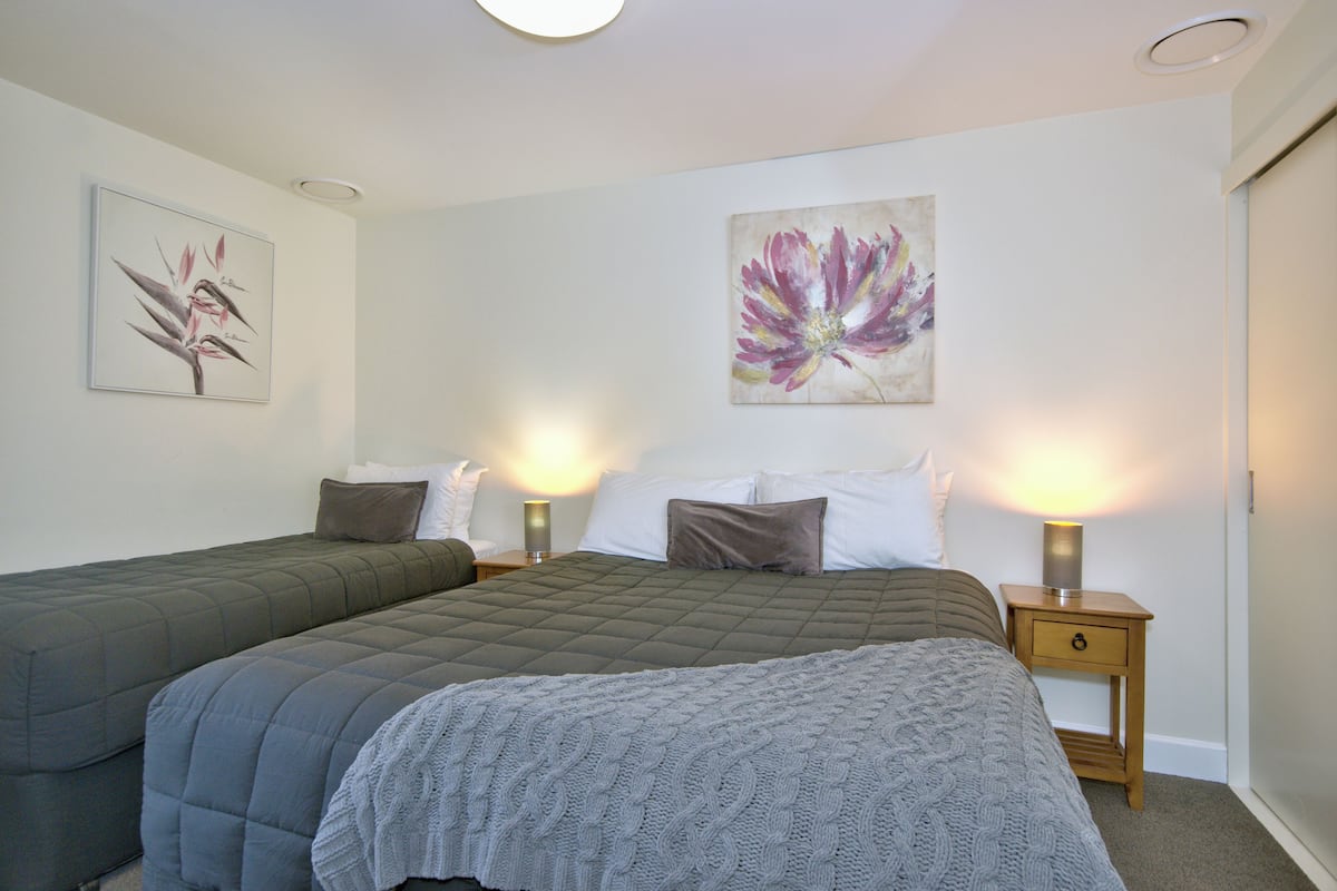 Quarto com duas camas, uma mesa de cabeceira com abajur e duas pinturas penduradas na parede.