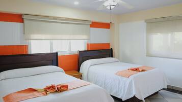 Quarto de hotel com duas camas, ventoinha no teto e janela com cortinas.
