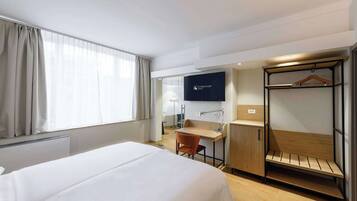 Quarto de hotel com cama, escrivaninha, cadeira, televisão e closet espaçoso.