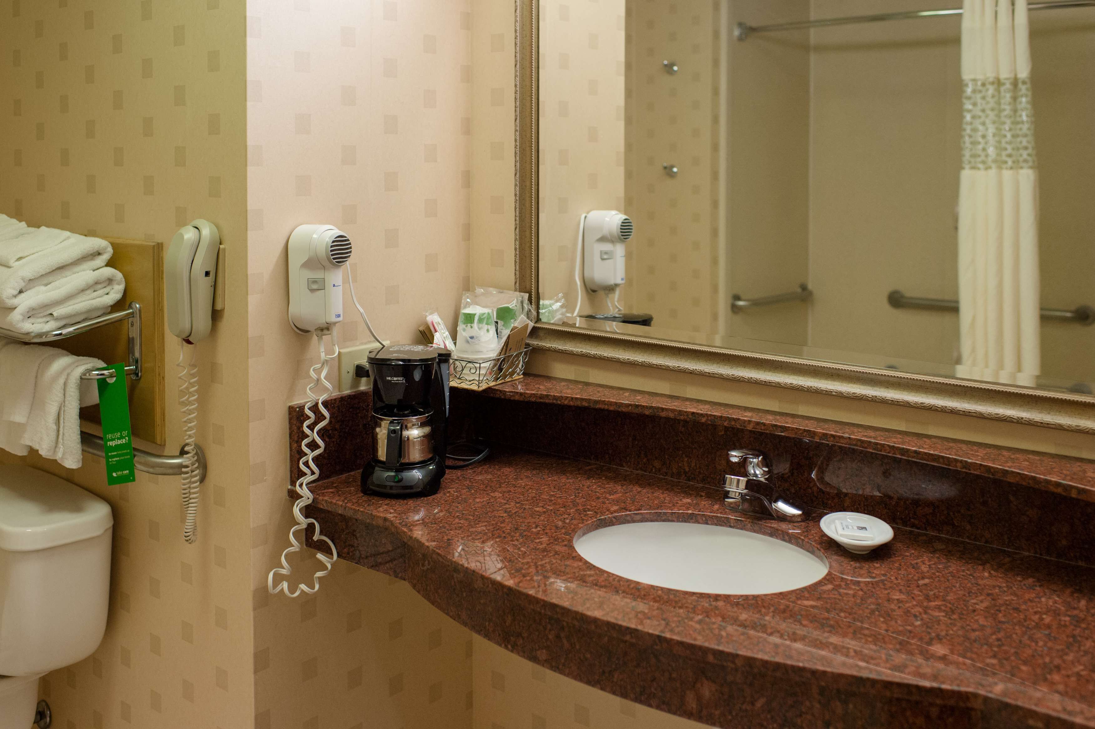 Casa de banho com lavatório, espelho, suporte para toalhas, secador de cabelo e máquina de café.