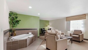 Quarto de hotel com uma banheira grande, sofás bege, uma mesa de centro e um espaço de refeições com cadeiras.
