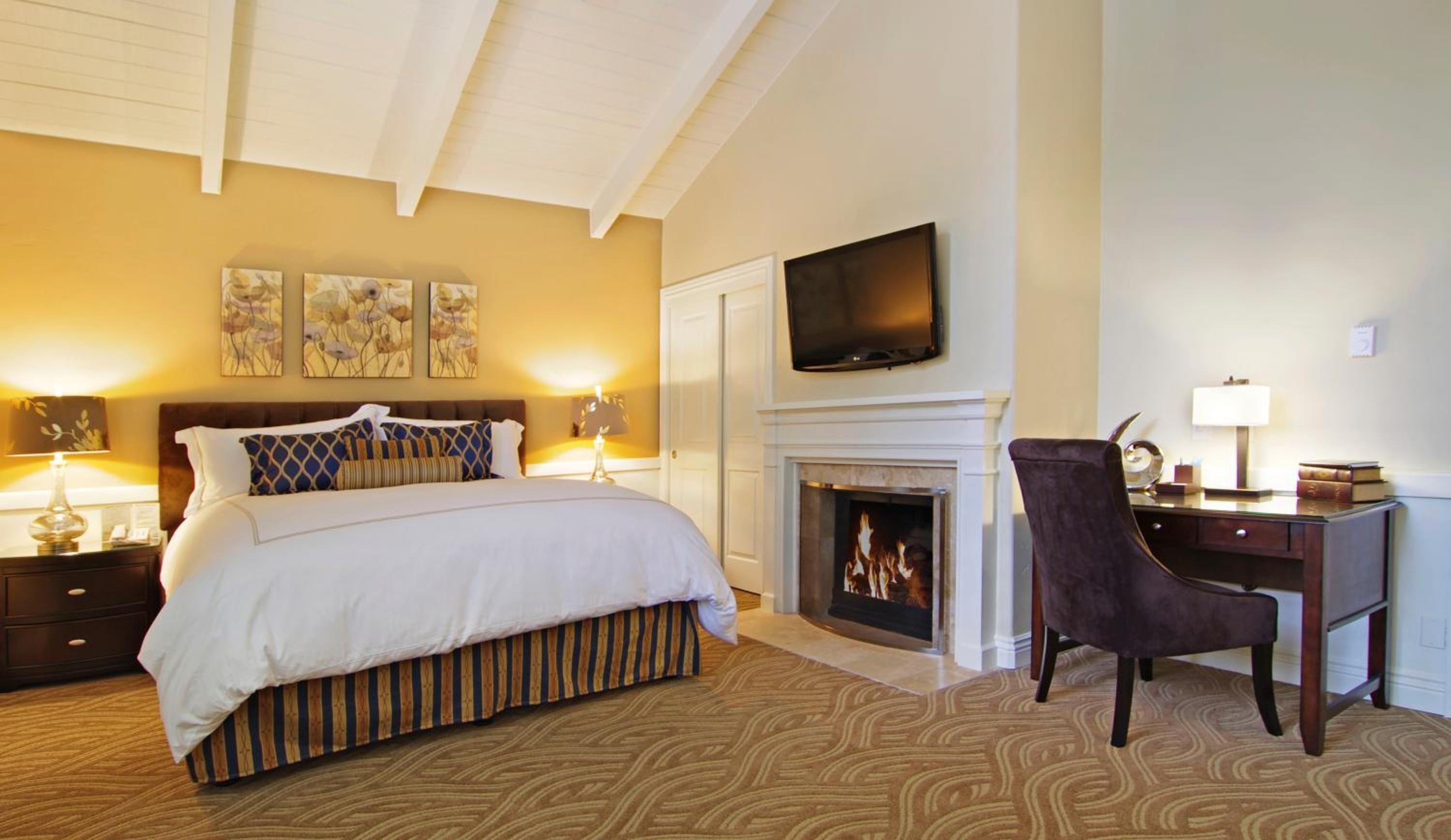 Quarto de hotel com uma cama grande, lareira, escrivaninha e obras de arte nas paredes.