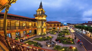 Um edifício histórico com uma torre central, um pátio com uma fonte e uma rua com pedestres.