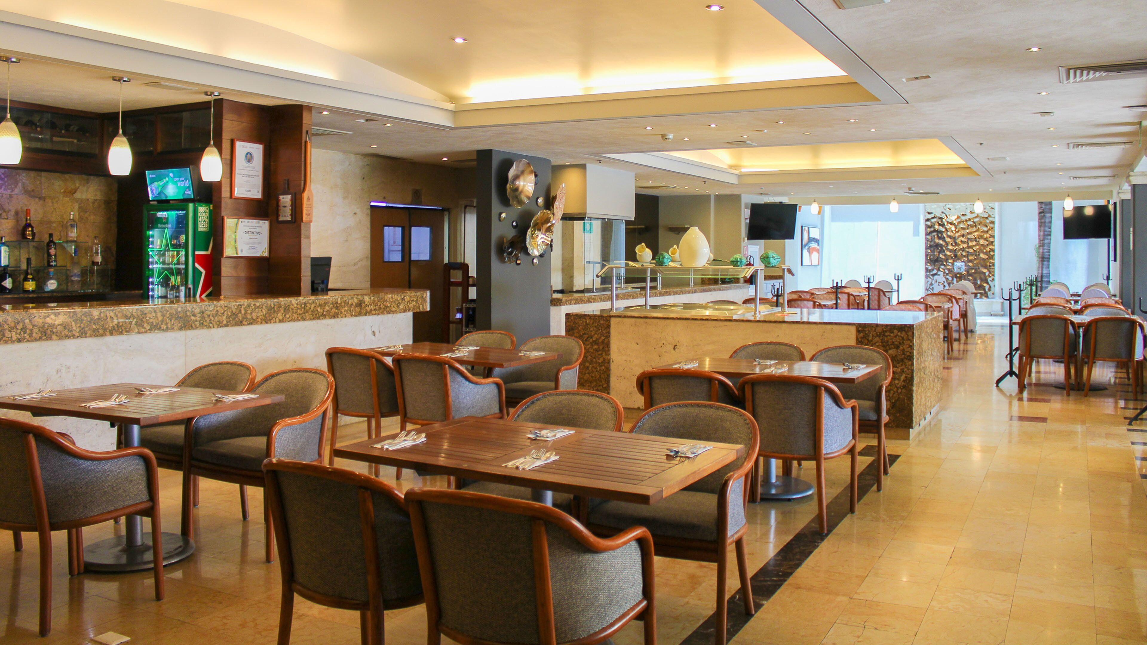 Um restaurante espaçoso com várias mesas e cadeiras, área de bar com balcão e uma grande parede decorativa.