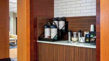 Uma área de recepção de hotel com um espaço de café, um balcão e uma área de estar ao fundo.