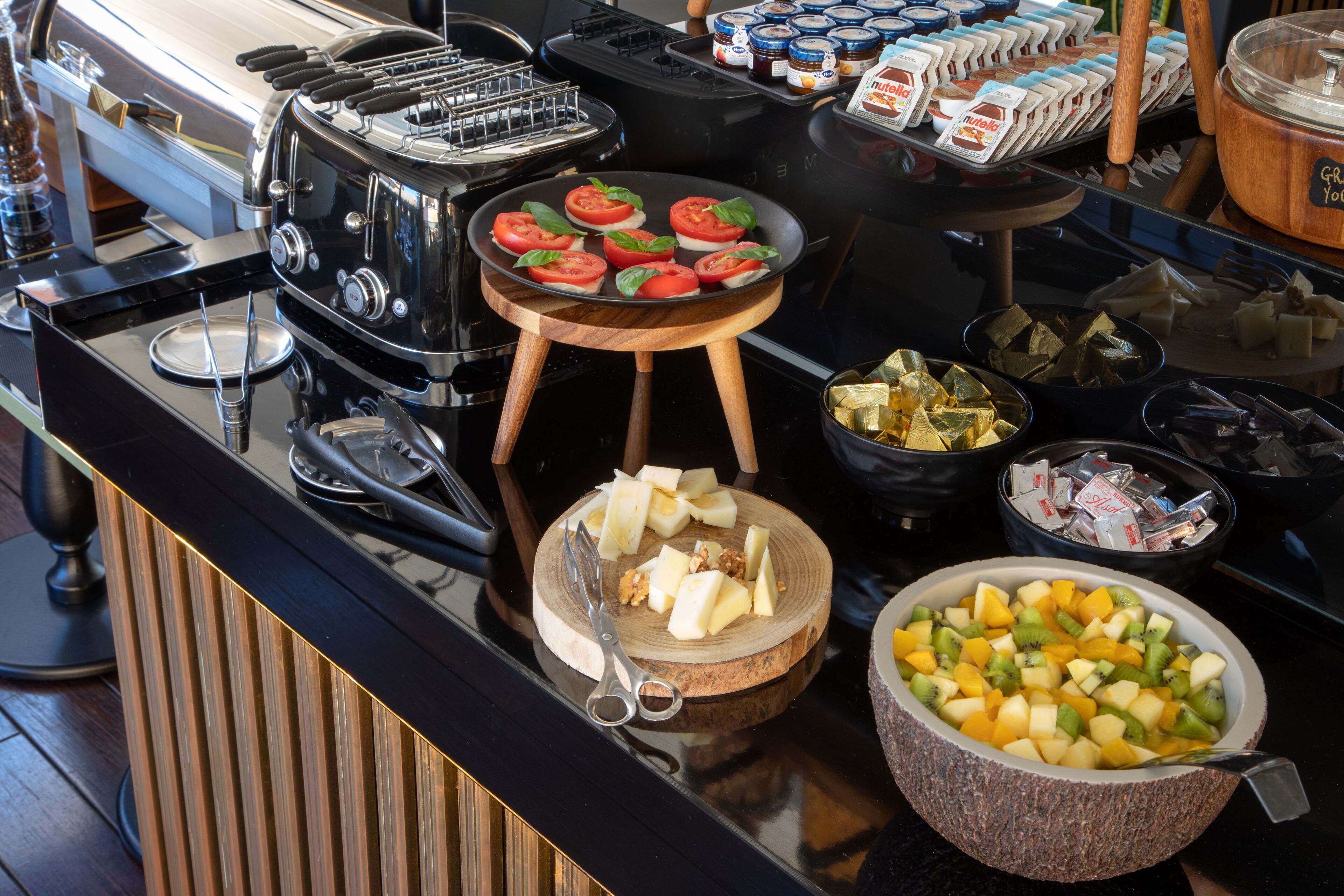 Buffet com diversos alimentos, incluindo tomates fatiados, queijo e uma tigela de frutas mistas.